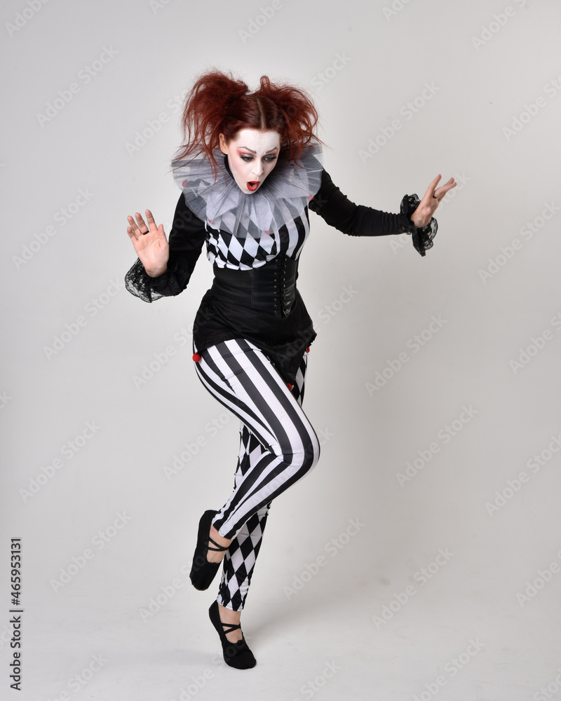 Full length portrait of red haired girl wearing a black and white clown ...