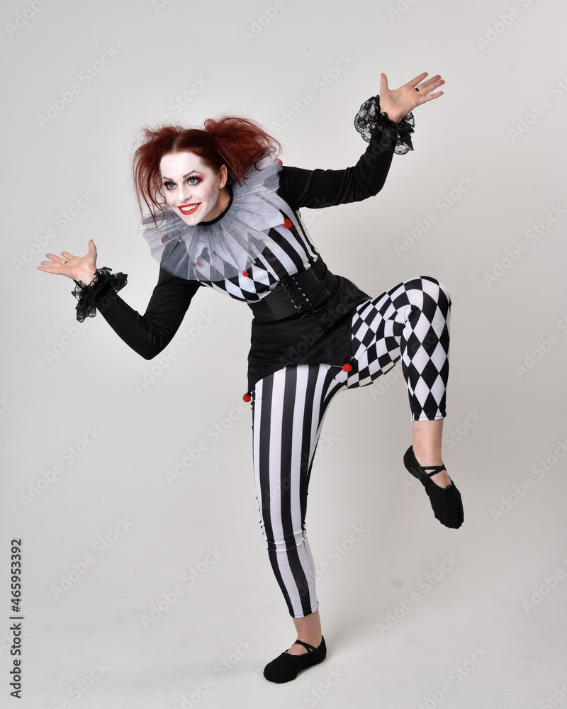 Full length portrait of red haired girl wearing a black and white clown ...