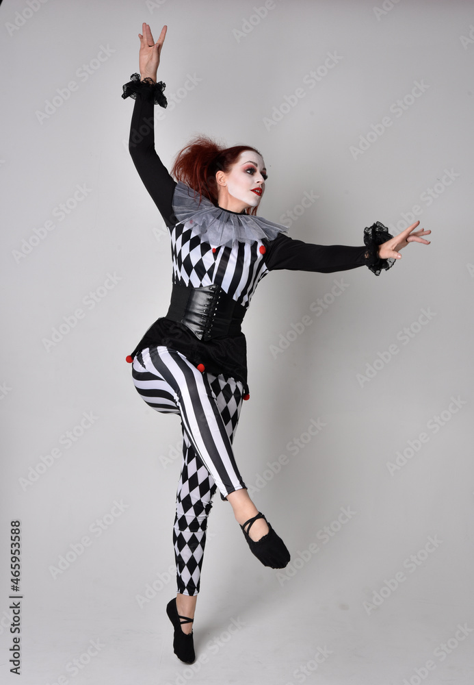 Full length portrait of red haired girl wearing a black and white clown ...