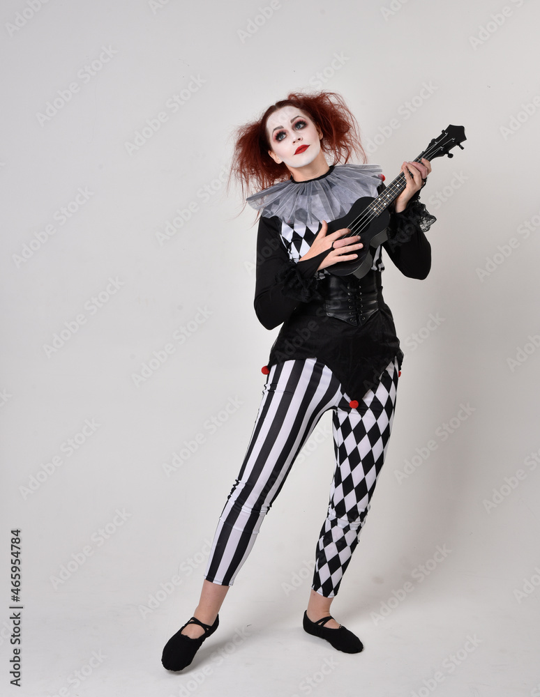Full length portrait of red haired girl wearing a black and white clown ...