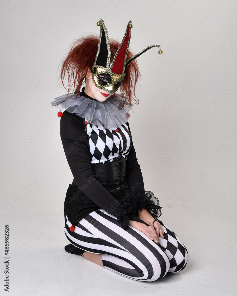 Full length portrait of red haired girl wearing a black and white clown ...