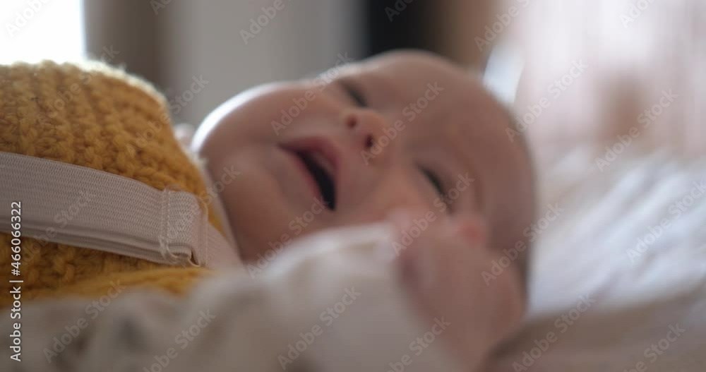 The baby is lying on the bed, whimpering and floundering with its arm ...