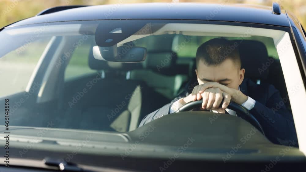 Exhausted male driver holding head in steering wheel while sitting in ...