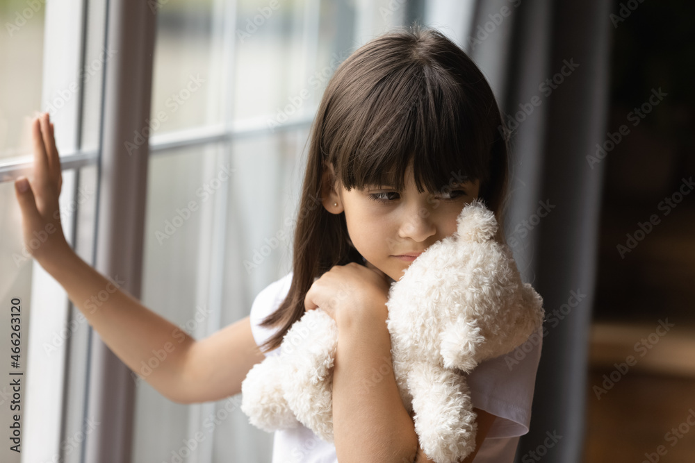 Sad lonely kid holding, hugging teddy bear toy, standing at window ...