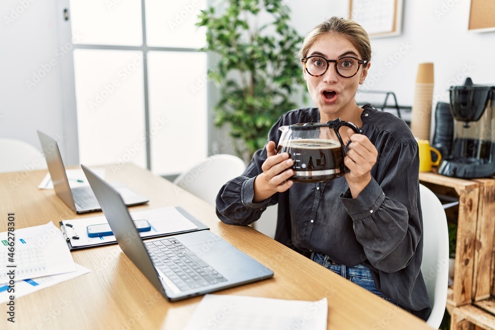 Young blonde woman working at the office holding coffee pot scared and ...