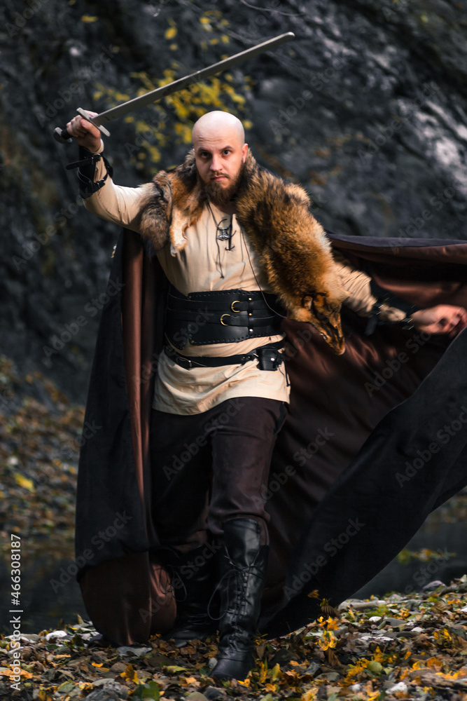 A handsome bearded man in a medieval cloak with a sword in his hands ...
