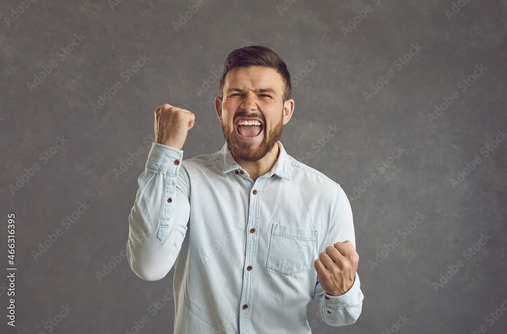 Portrait of an emotional young man laughing and shouting with clenched ...