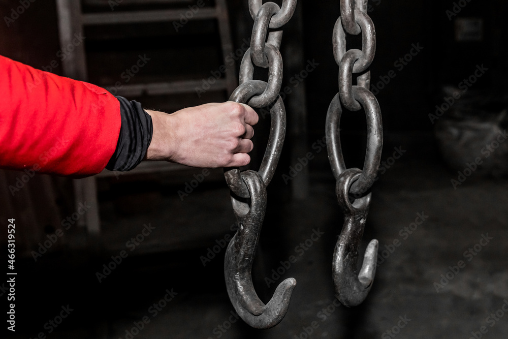 The hand of a male worker holds an iron chain with a hook lifting ...