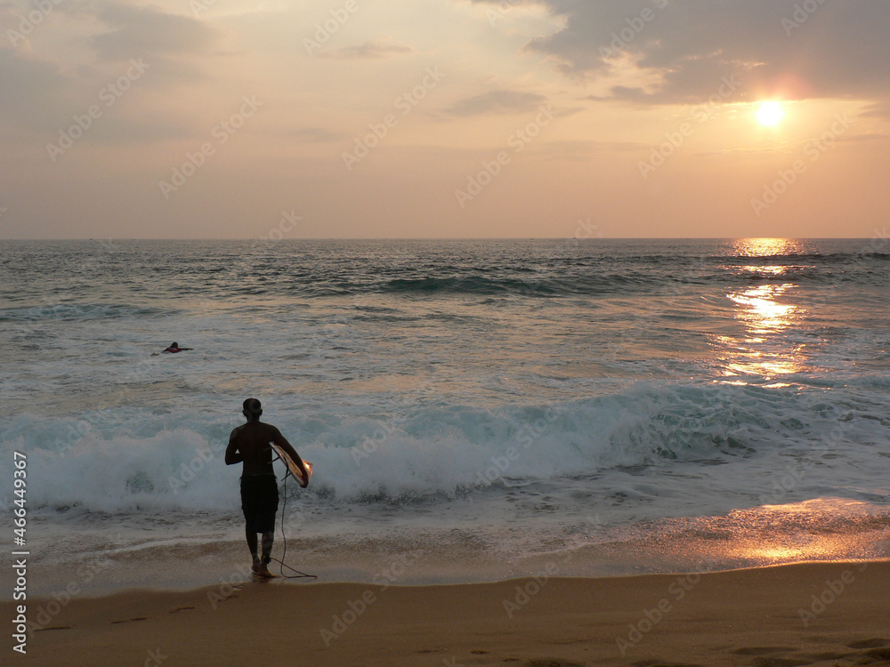 Back view of a man with a surfing board on the Hikkaduwa beach ready to ...