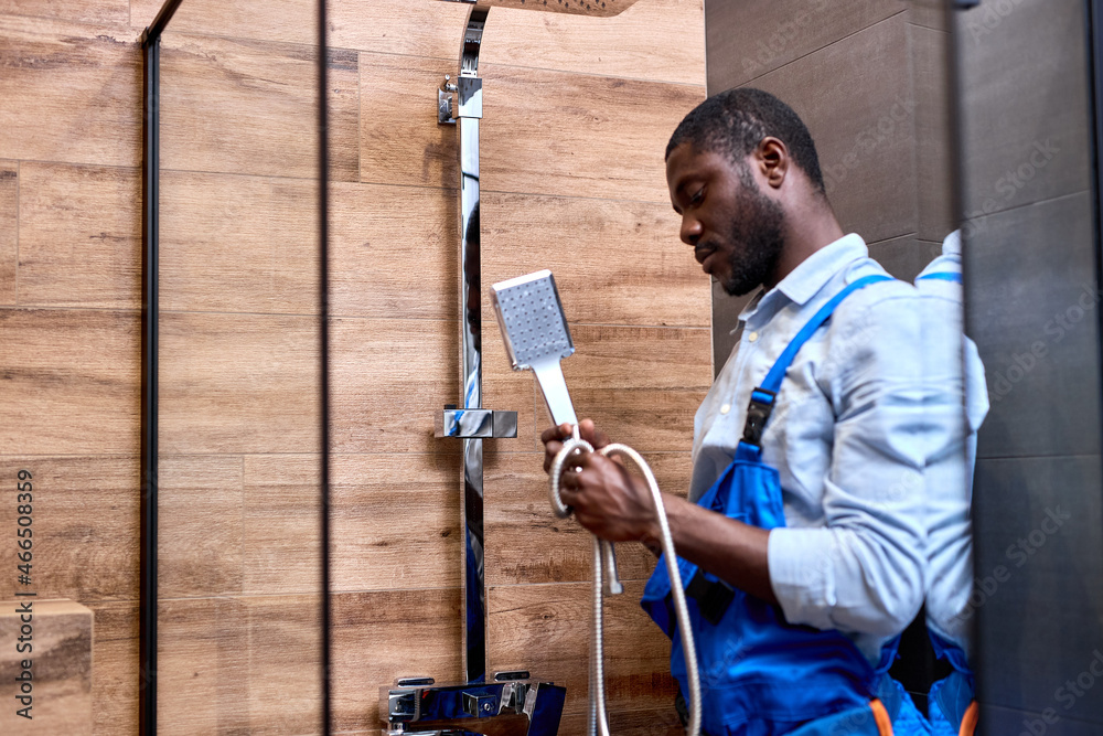 Side view on black repairman handyman in blue overalls holding shower ...