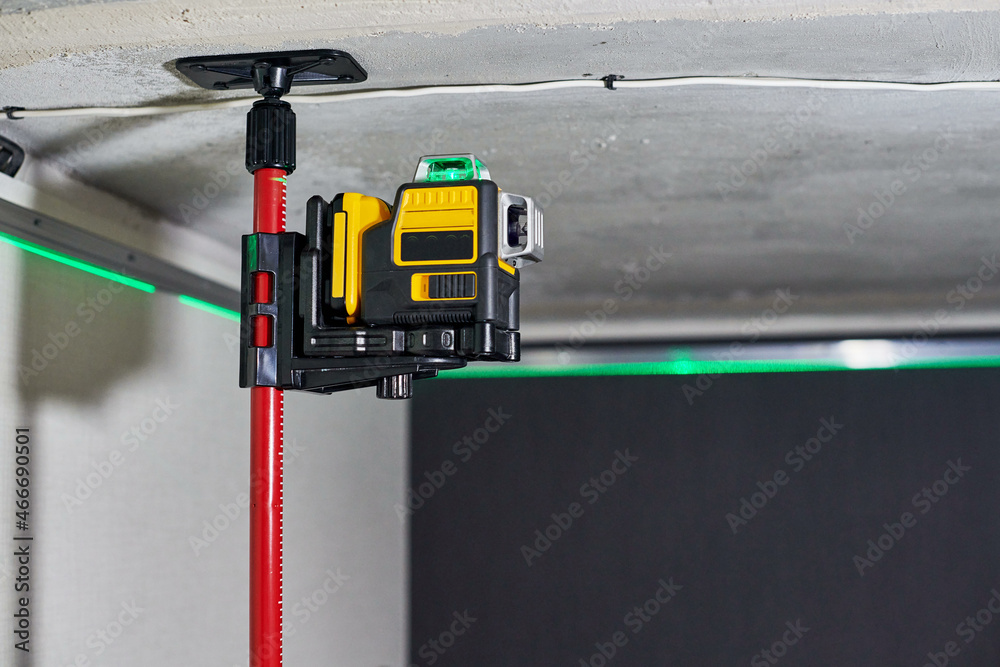 Laser level measuring tool with visible green laser beam on wall of ...