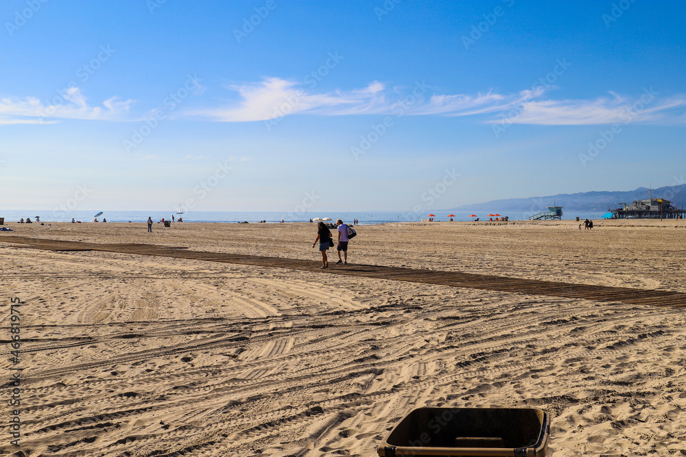 a man and a woman walking down a wooden boardwalk in the sand at the ...