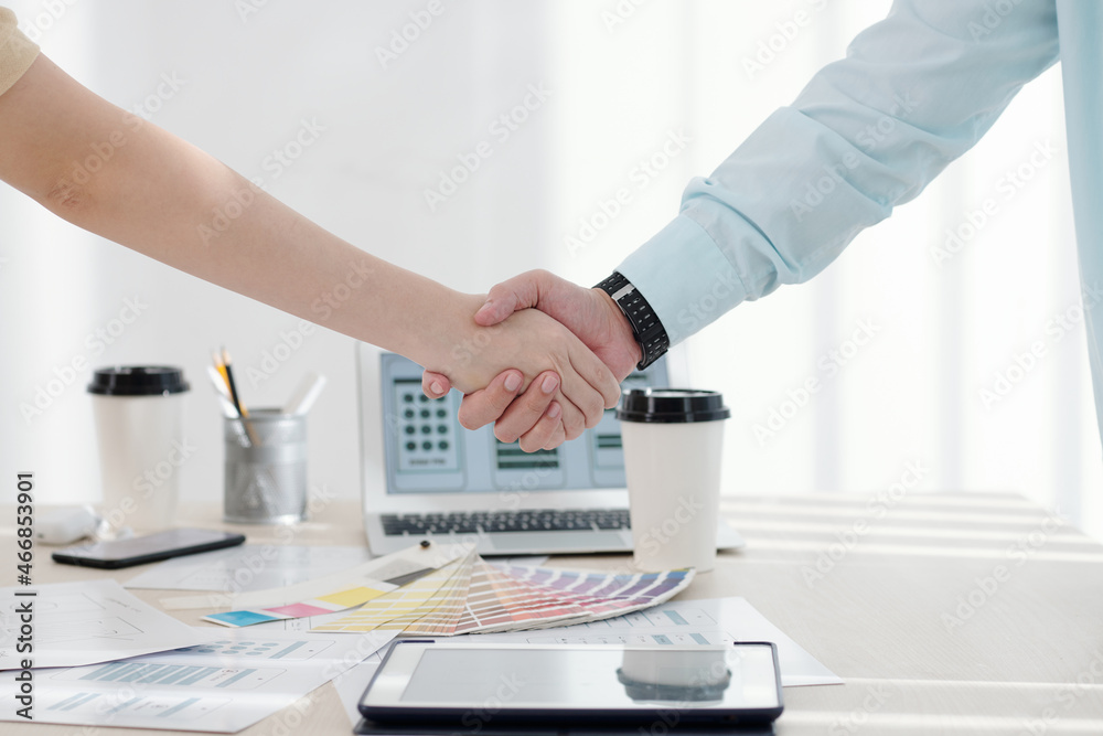 UI designer and client shaking hands over table with mockups, sketches ...
