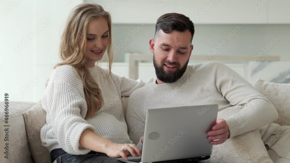 Happy young couple is using a laptop together, sitting at home on a ...