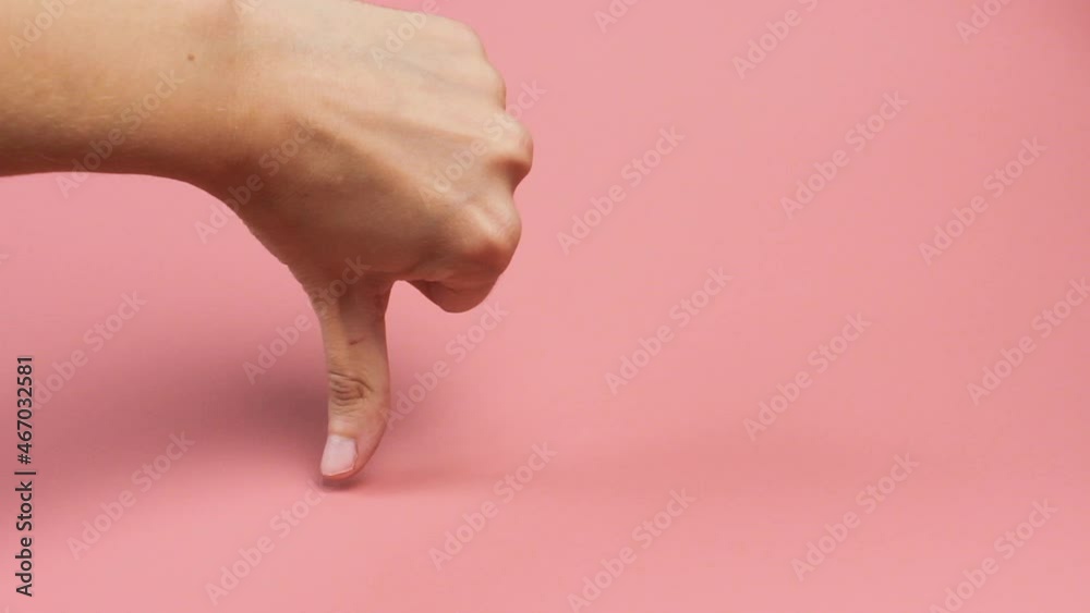 Woman's hand with a thumb up puts a finger down on a pink background ...