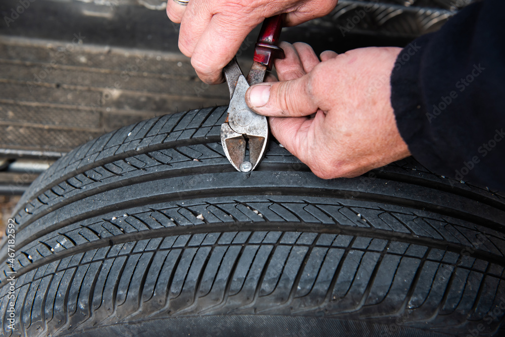 mechanic's hands removing a screw from the punctured wheel with pliers ...