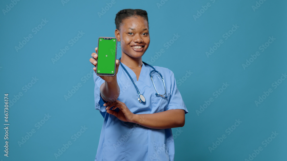 Smiling nurse showing green screen on mobile phone at camera. Medical ...