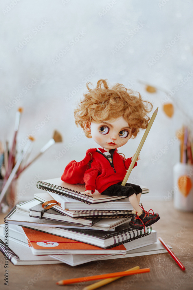 A puppet boy sits on the artist's desk with a pencil in his hand on a ...