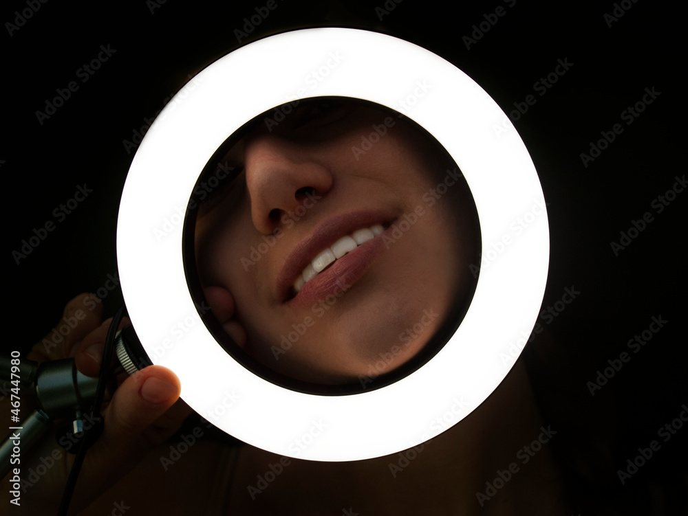 A beautiful young girl with looks out from behind a circular lamp for ...