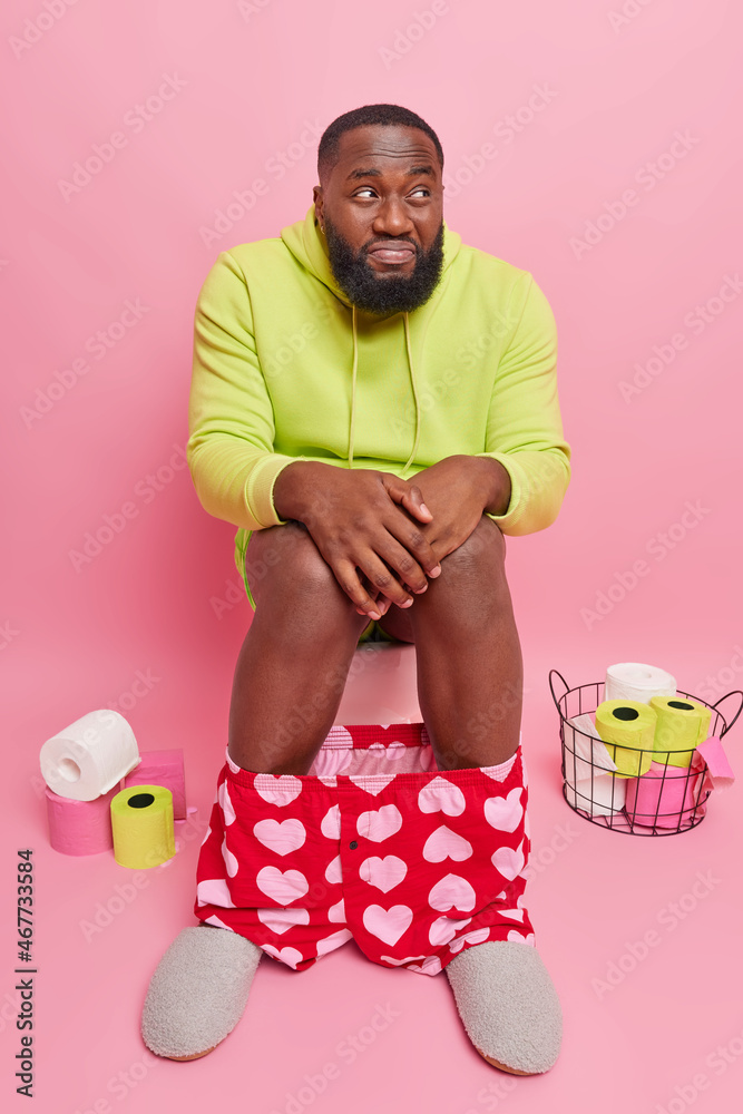 Vertical shot of black bearded man sits on toilet in bathroom at ...