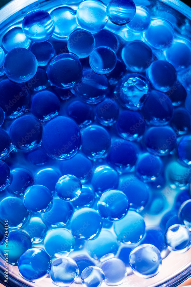 Blue water beads in a clear glass bowl in cold water with a reflection ...