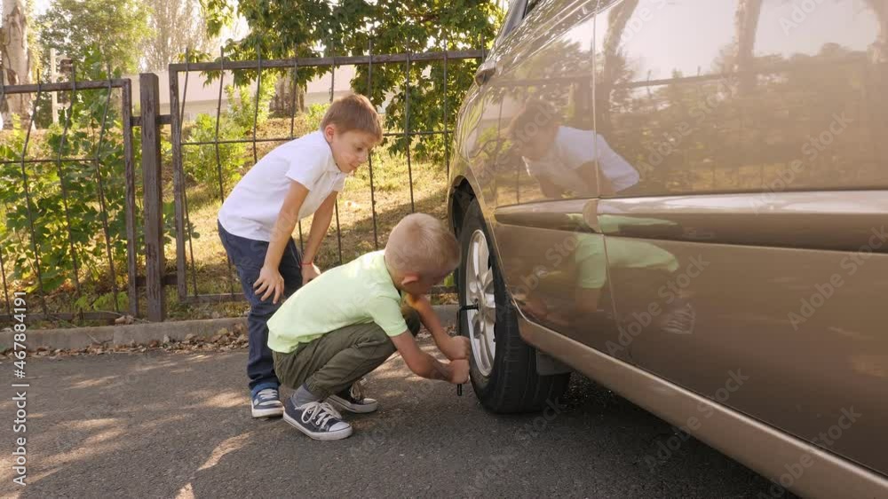 Two little brothers help Dad fix the car, they unscrew the bolts on the ...