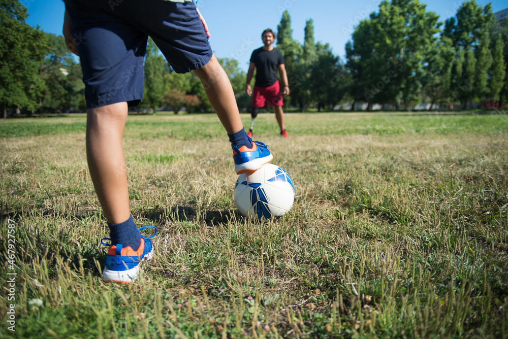 Father with prosthetic leg playing football with son in park. Man with ...