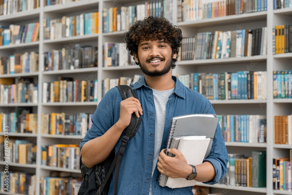 Cheerful male international student at university library or book store ...
