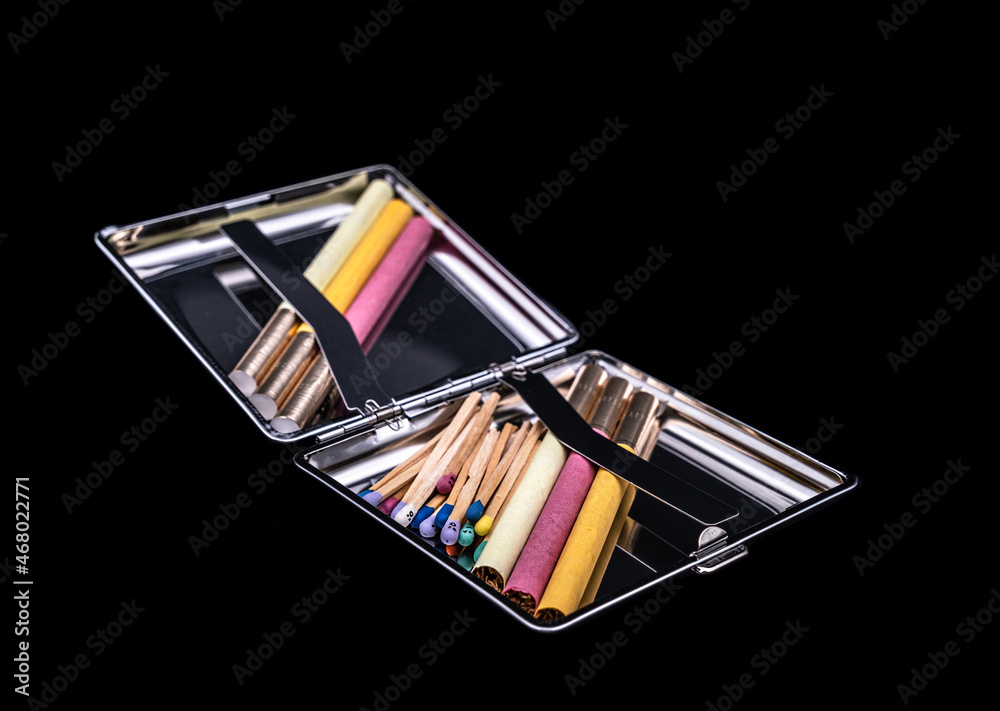 Metal tobacco box with color cigarettes and matchsticks on a black ...