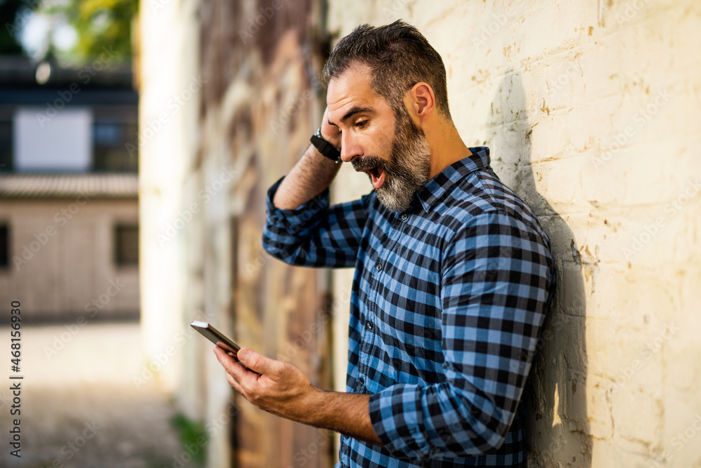 Shocked businessman with a beard looking at his phone while standing in ...