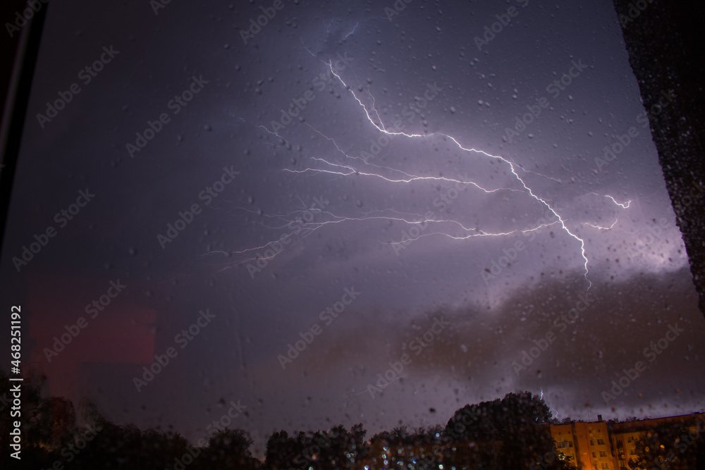 Lightning bolts striking in the dark cloudy night sky through a wet ...
