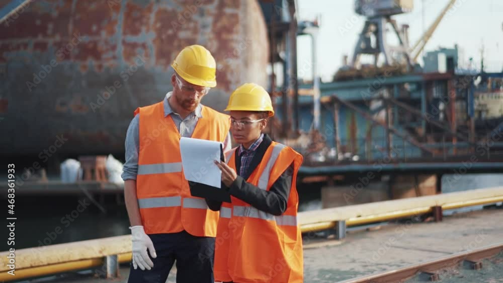Two shipbuilders discussing a working project and writing in notepad ...