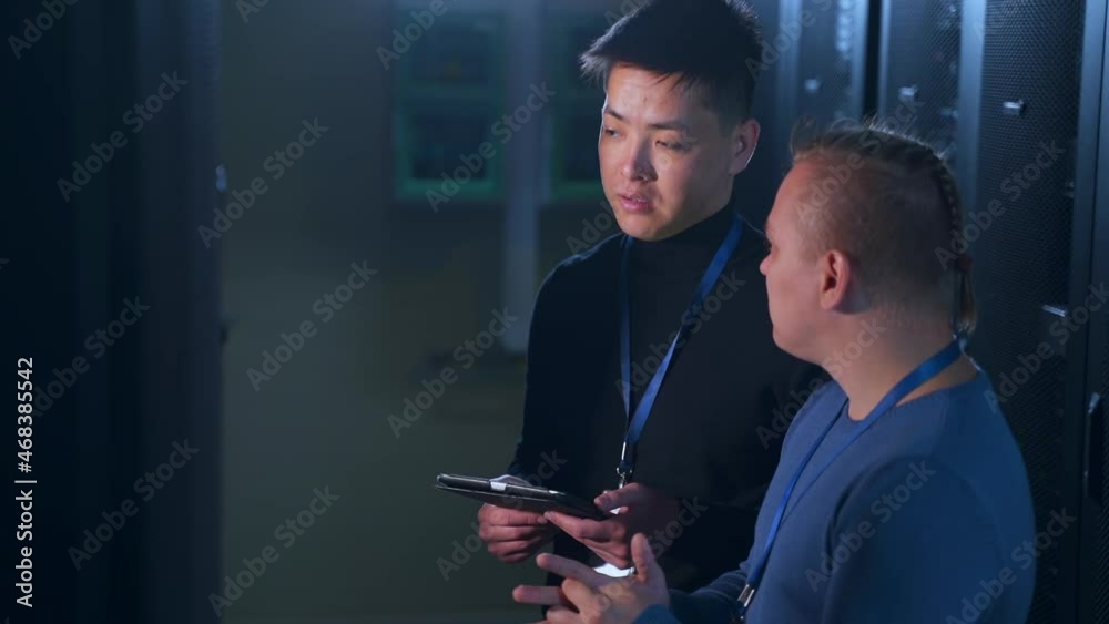 Multi-ethnic team of engineers talking and checking server racks in big ...