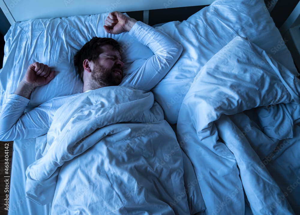 Man in white pajamas has a terrible nightmare, wrinkles face and ...
