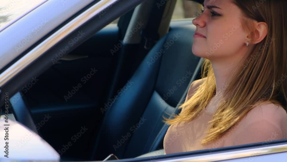 An upset frustrated young woman beats the steering wheel of a car with ...