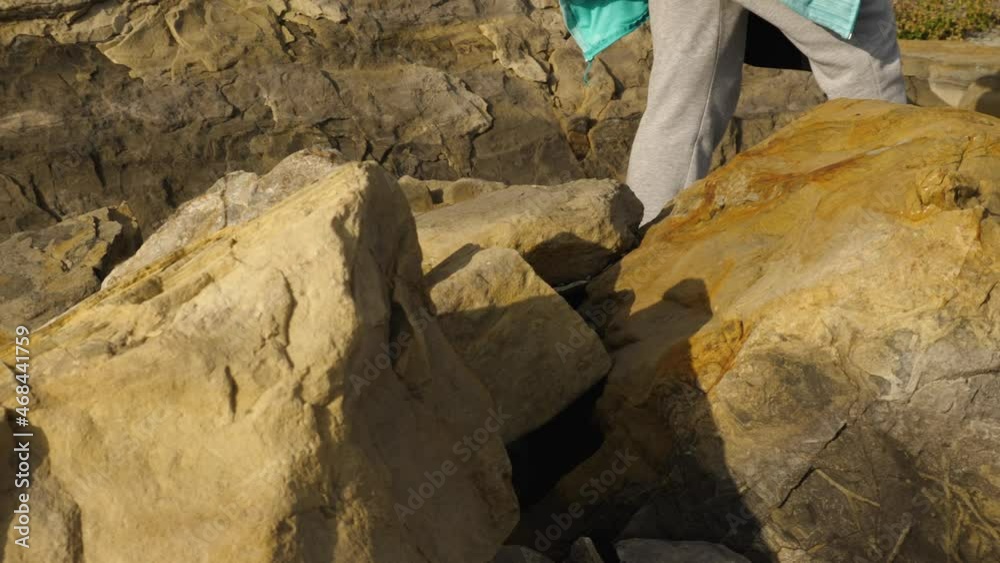 Women's legs in pants and sneakers walk on the rocks against a backdrop ...