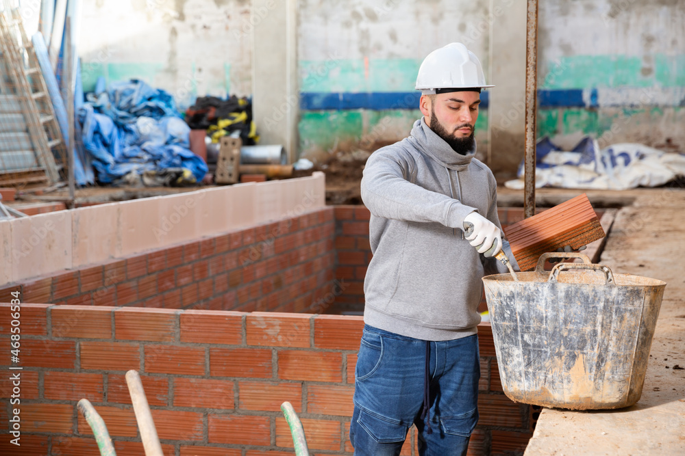 Confident young builder working with red brick on overhauls of house ...