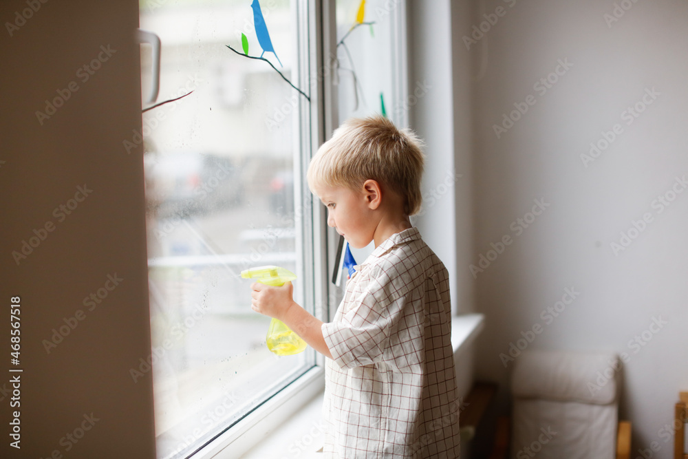 Cute boy toddler blond toddler at the window washes the glass. Helping ...