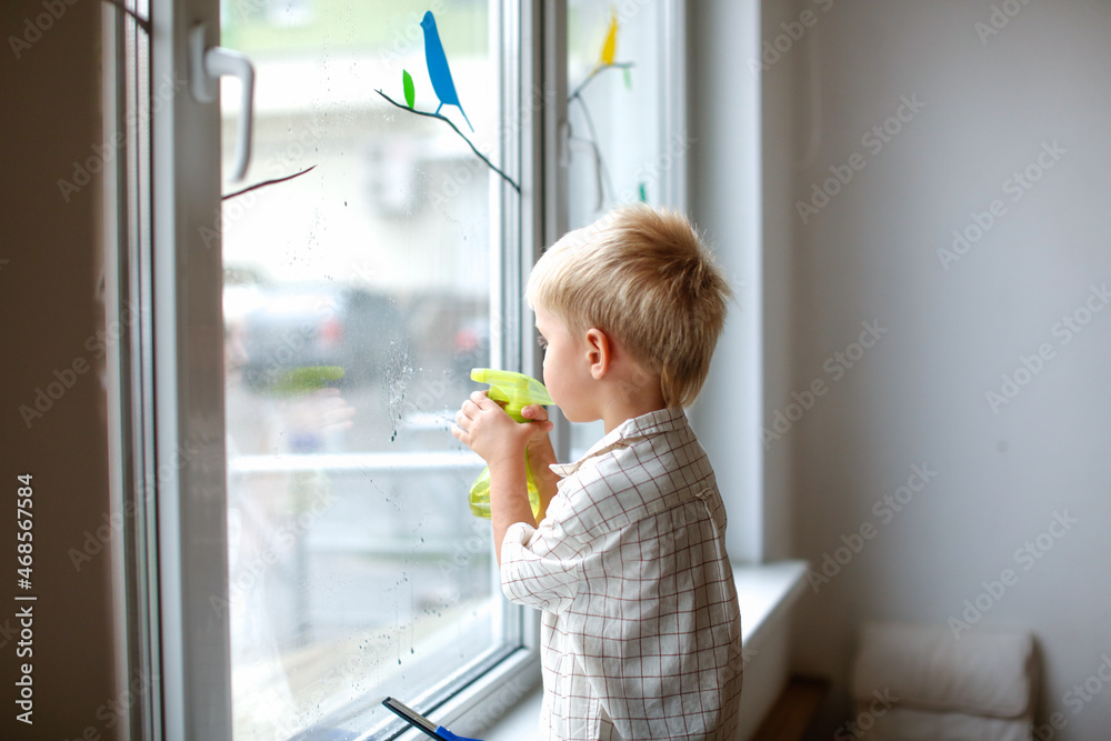 Cute boy toddler blond toddler at the window washes the glass. Helping ...