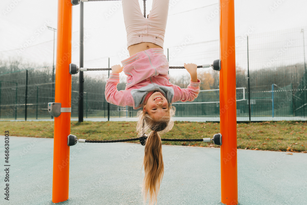 A young girl on a climbing frame hangs upside down on a children's ...