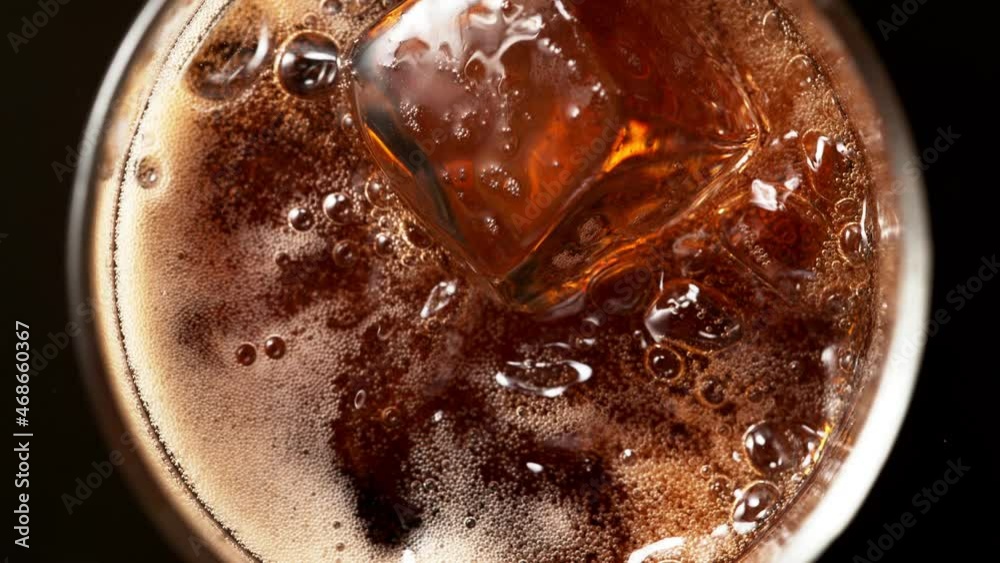 Super slow motion of falling ice cube into cola drink, top view. Filmed ...