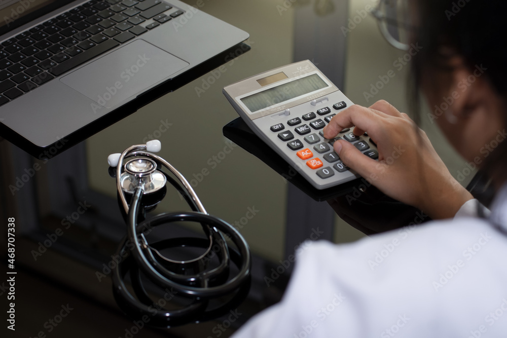Female doctor with stethoscope using calculator and work on laptop ...