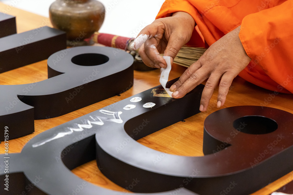 Thai monk to bless by making marks on the sign with golden leaf for ...