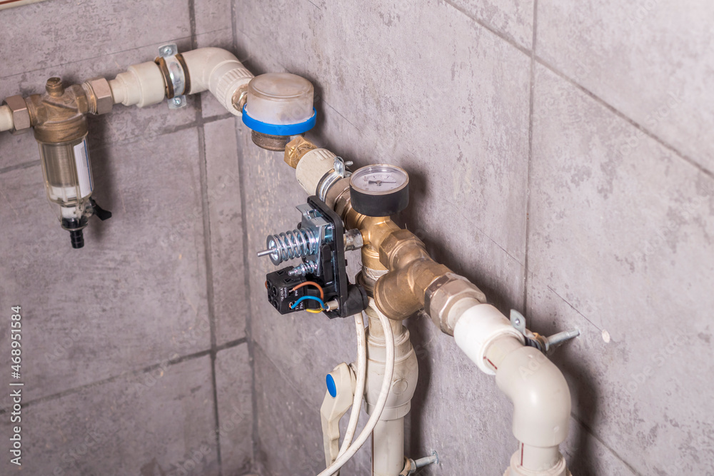 there is a pipe with water on the tiled wall. a water meter is also ...