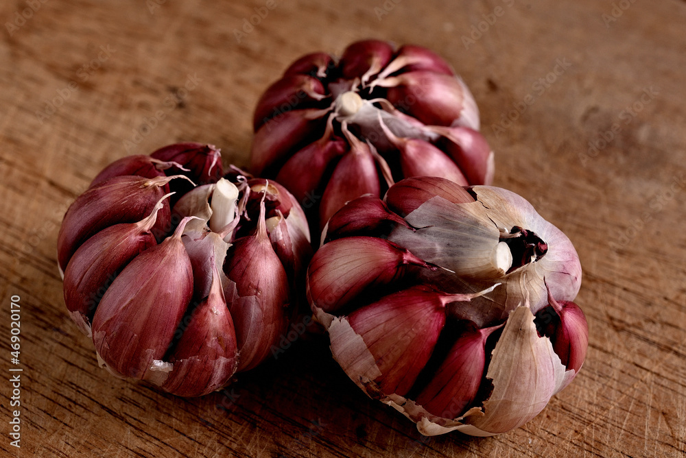 Cabeçãs de alho roxo na tabua de madeira rústica com iluminação lateral ...