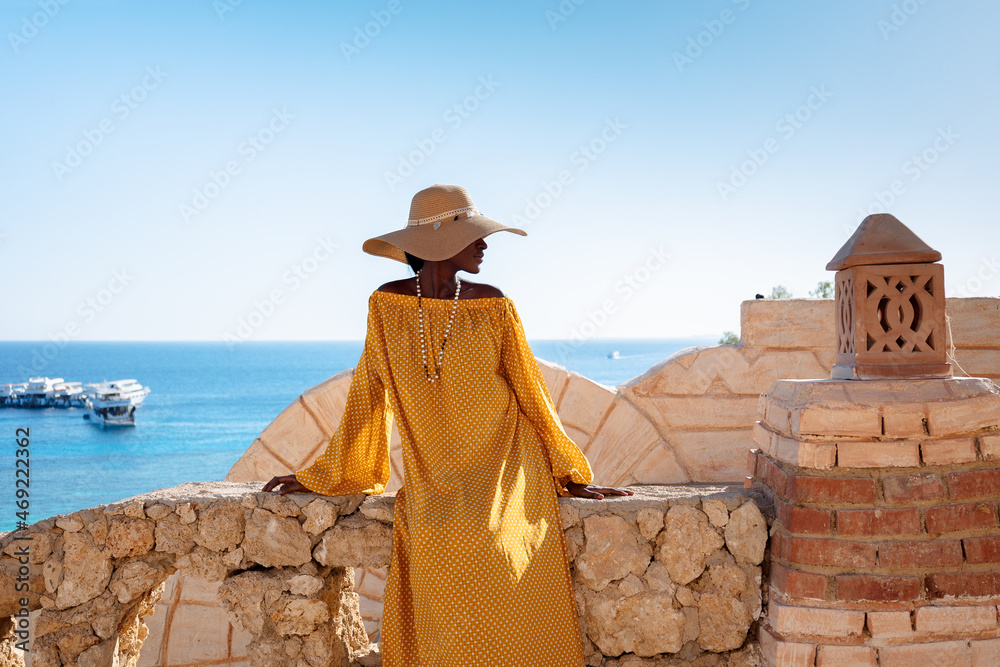 Happy African American woman in yellow dress and sun hat enjoys view of ...