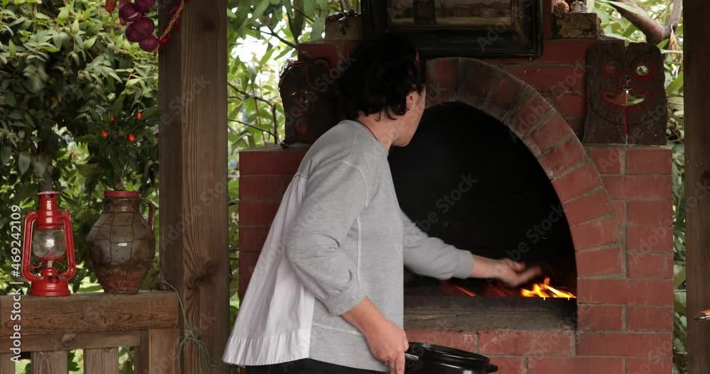 Woman set on fire in fireplace and put glazed clay pot into rustic ...