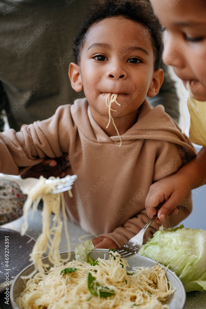 Cute boy eating spaghetti amidst brother and father in kitchen Stock ...