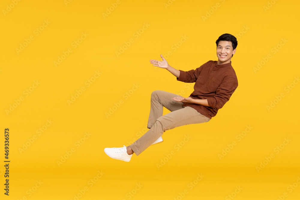Happy cheerful young Asian man floating in the air isolated on yellow ...