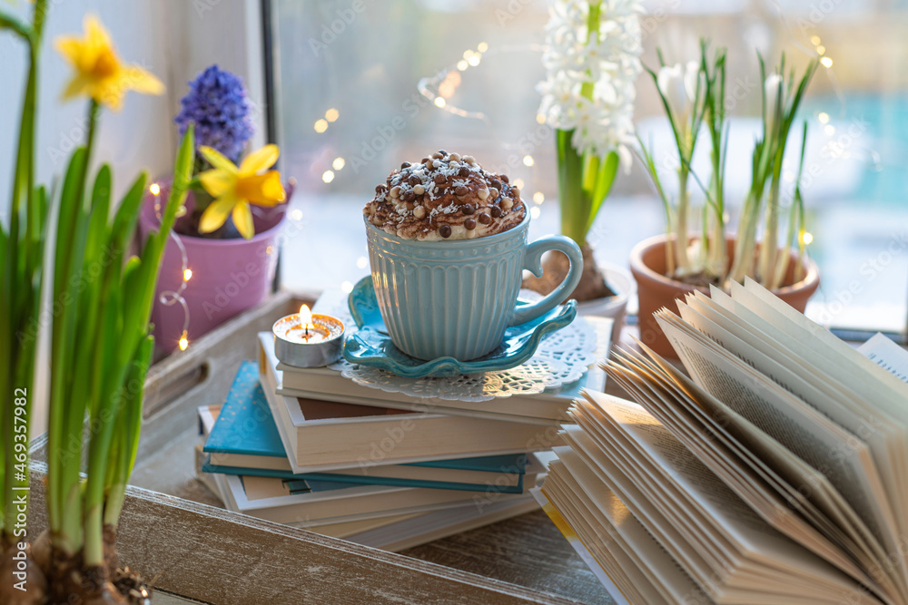 Coffee cup with whipped cream, spring flowers and open book on window ...